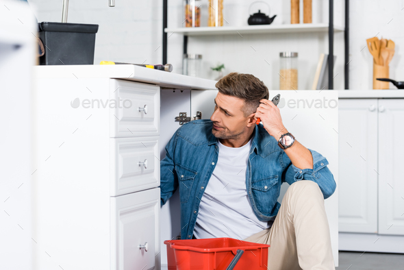 confused man sitting on floor while repairing kitchen sink Stock Photo ...