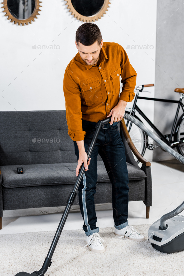 handsome man in modern living room cleaning house with hoover Stock ...
