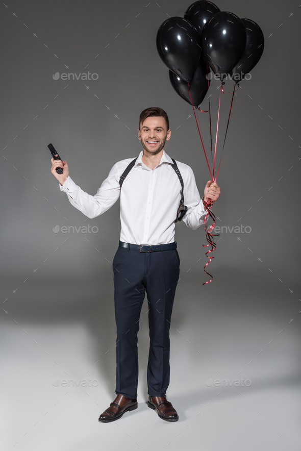 cheerful secret agent with holster holding gun and black balloons on ...