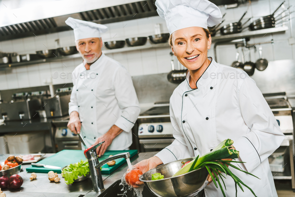 female and male chefs in double-breasted jackets and hats looking at ...