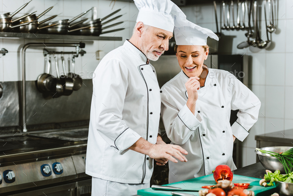 female and male chefs in uniform having conversation while cooking in ...