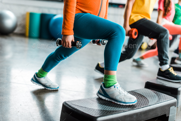 Cropped view of kids standing on step platforms and holding dumbbells ...