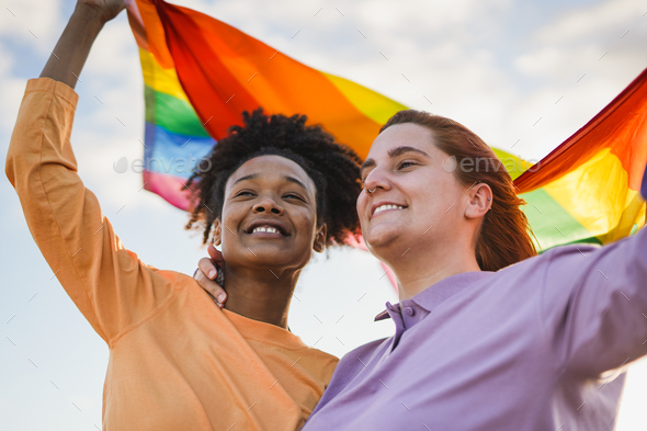 Young lesbian multiracial couple holding LGBT rainbow flag outdoor at ...