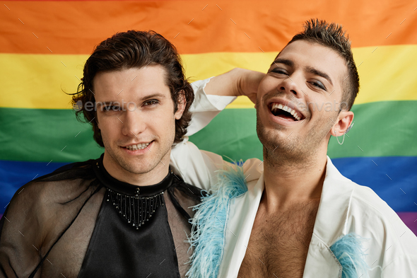 Two gay young men posing with LGBTQ pride flag in background Stock ...