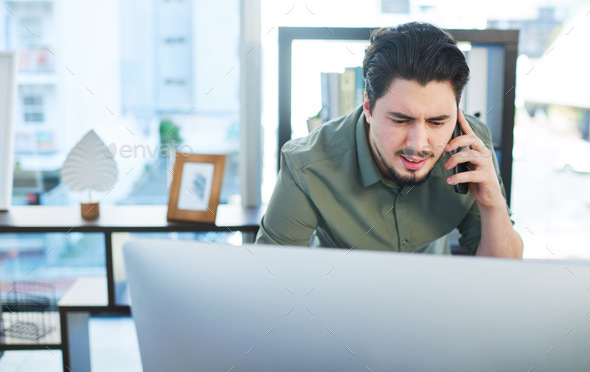 Shot of a young businessman using a computer while talking on a ...