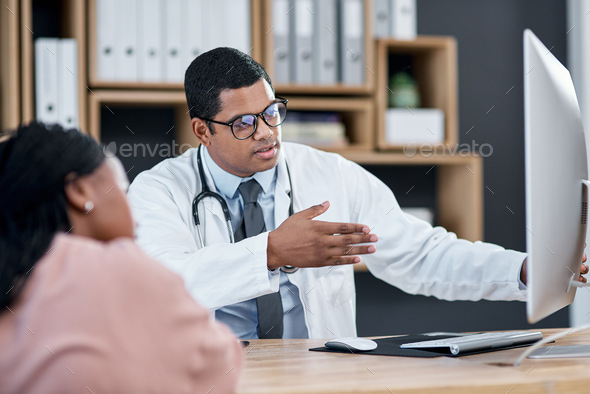 Shot of a doctor using a computer while having a consultation with a ...