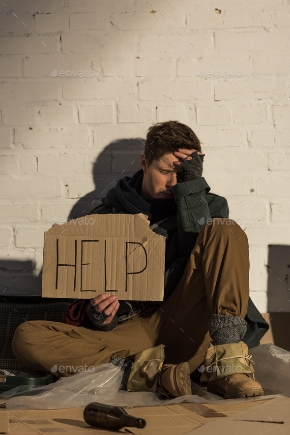 despaired homeless man sitting by brick wall and holding piece of ...