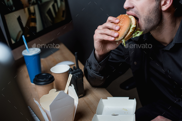 cropped view of guard eating burger at workplace Stock Photo by ...