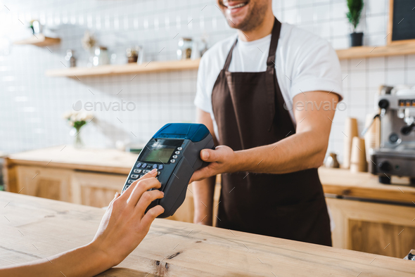 cropped view of cashier standing near bar counter and holding terminal ...
