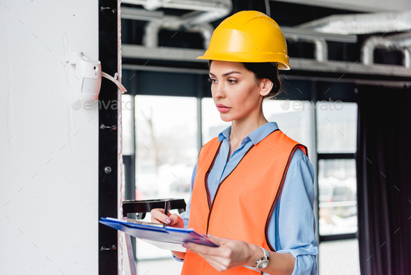 serious female firefighter standing near fire alarm while holding ...