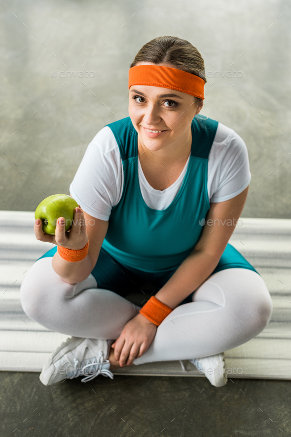 overhead view of happy plus size girl sitting on fitness mat with ...
