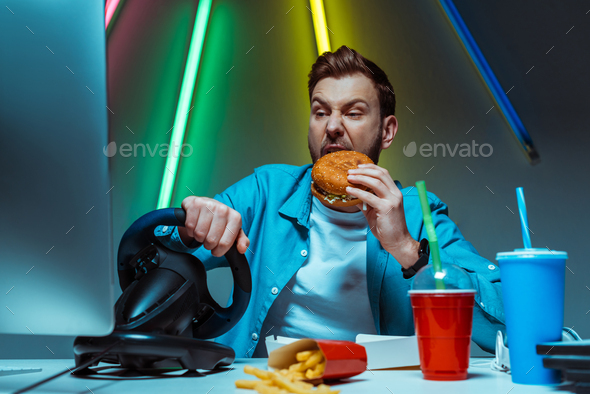 handsome and good-looking cyber sportsman eating burger and playing ...
