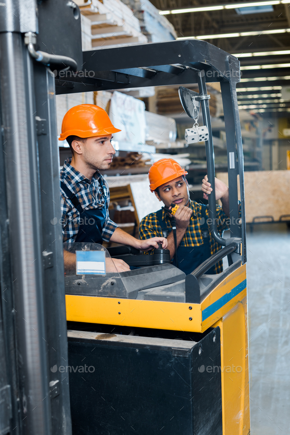 handsome, attentive worker in helmet sitting in forklift machine near ...