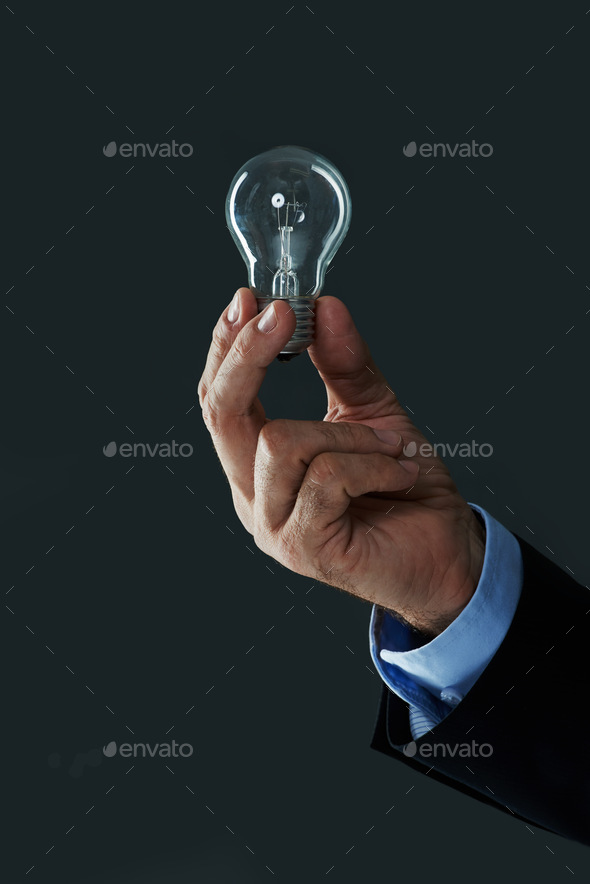 I need a good idea. Shot of a hand holding a lightbulb on a black ...