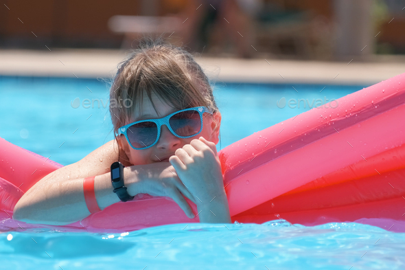 Young joyful child girl having fun swimming on inflatable air mattress ...