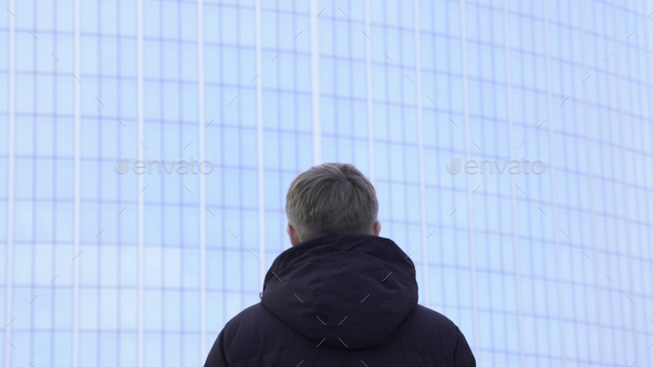 Rear view of man looking at glass building. Media. Man stands and looks ...