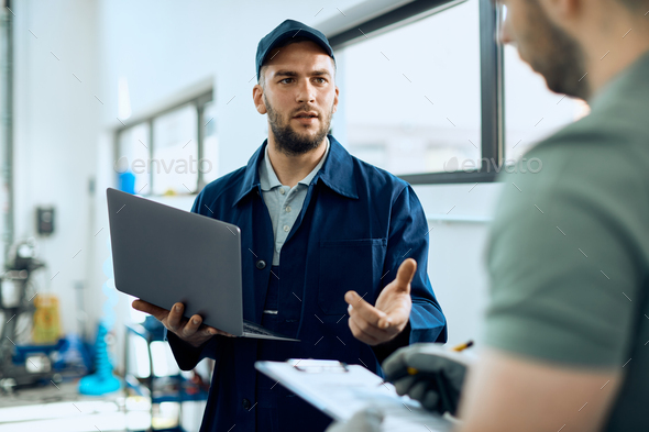 Car mechanic using computer while giving instructions to his coworker ...