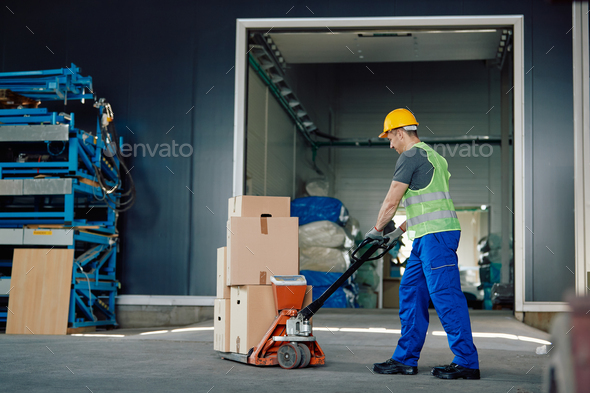Male worker pushing packages on pallet jack while working warehouse ...