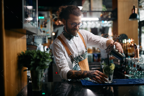 Happy bartender pouring cocktail from a shaker at bar counter. Stock ...