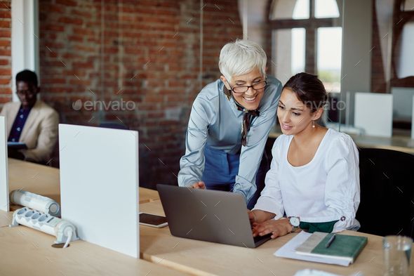 Happy senior CEO and her younger colleague working on laptop at ...