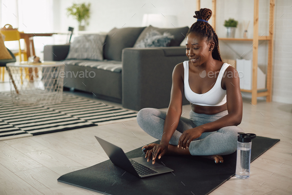 Happy black female athlete using laptop while during her water break at ...