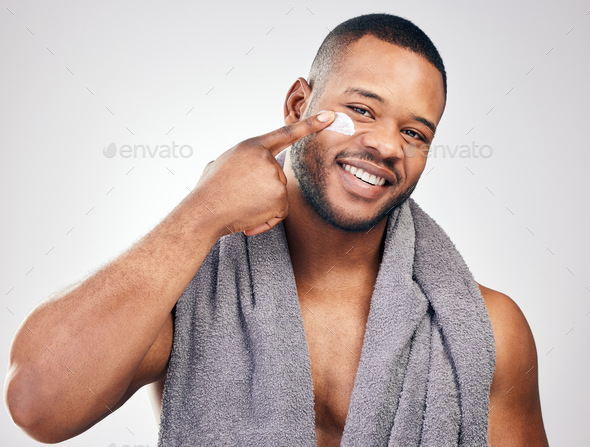 Studio portrait of a handsome young man applying moisturiser to his ...