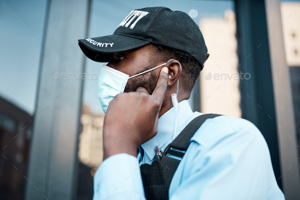 Shot of a masked young security guard using an earpiece while on patrol ...