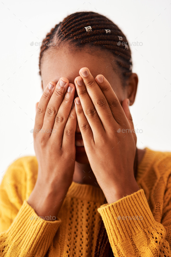 Studio shot of a woman holding her hands over her face while standing ...