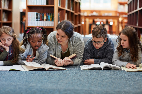 Cropped shot of elementary school kids reading with their teacher on ...
