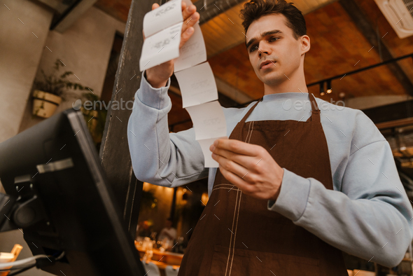 Young waiter man standing in front of computer and holding receipt ...