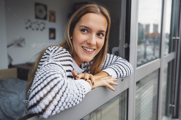 Smiling woman student looking out her dorm room window Stock Photo by ...