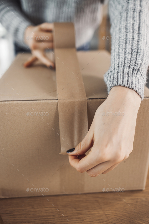 Unrecognizable woman hands taping a card board box with brown recycled ...