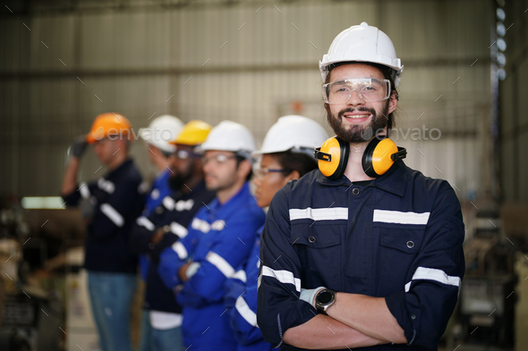Young confident leader of team standing in front of factory workers ...
