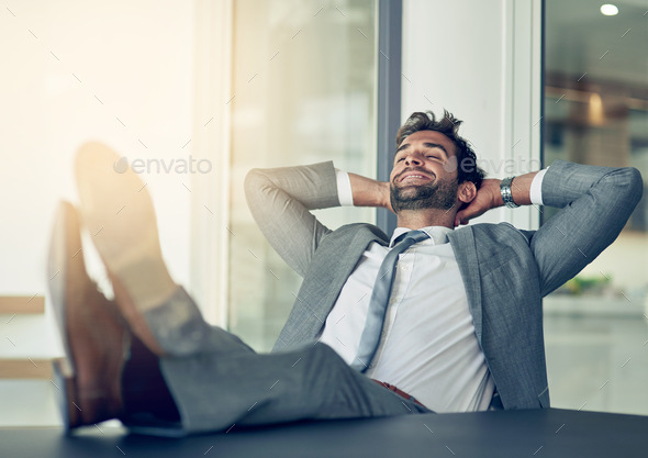 Shot of a businessman leaning back in his chair with his feet on a desk ...