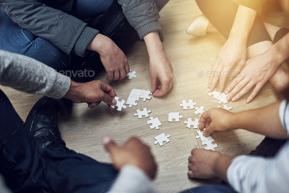 Start small and grow. Shot of a group of people building a puzzle ...