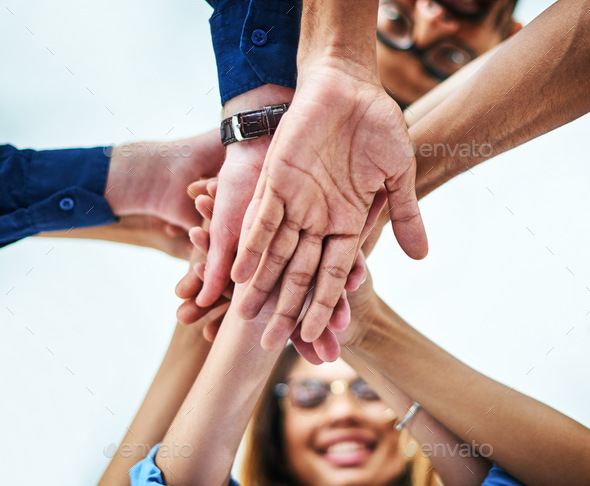 Low angle shot of a group of unrecognizable businesspeople joining their hands together in unity ...