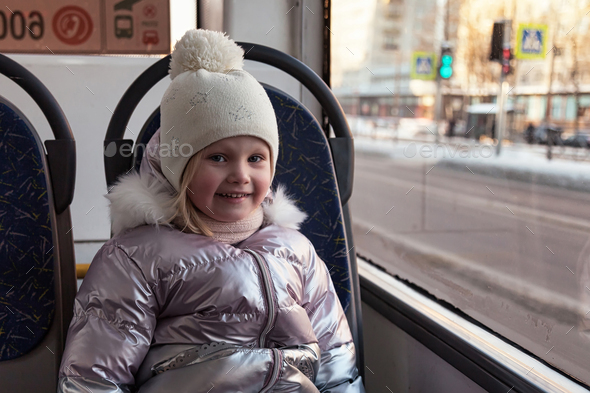 Little girl rides bus at window of public transport, looking at camera ...