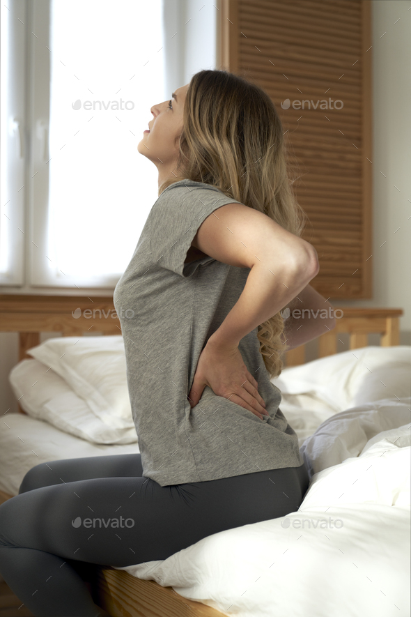 Caucasian woman with huge pain of loins sitting on the bed at home ...