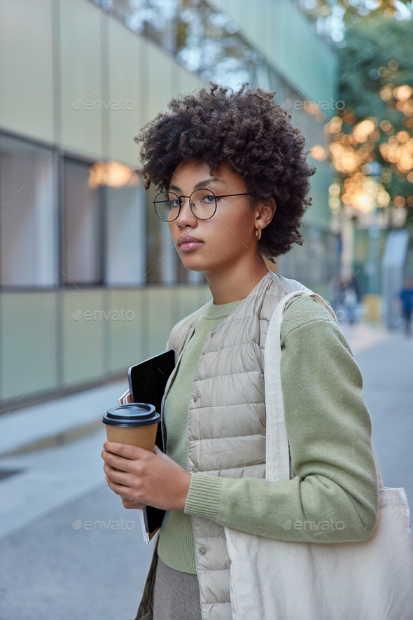 Vertical shot of pensive European millennial girl with takeaway coffee ...