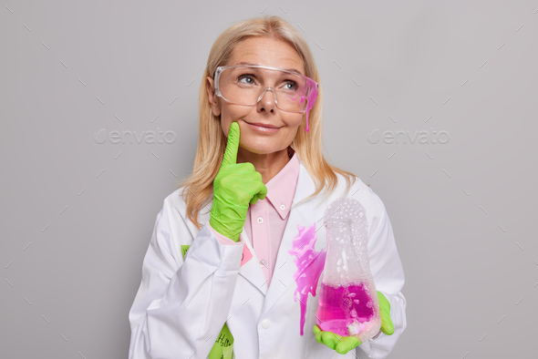 Thoughtful female researcher holds flask with pink liquid bubbles keeps ...