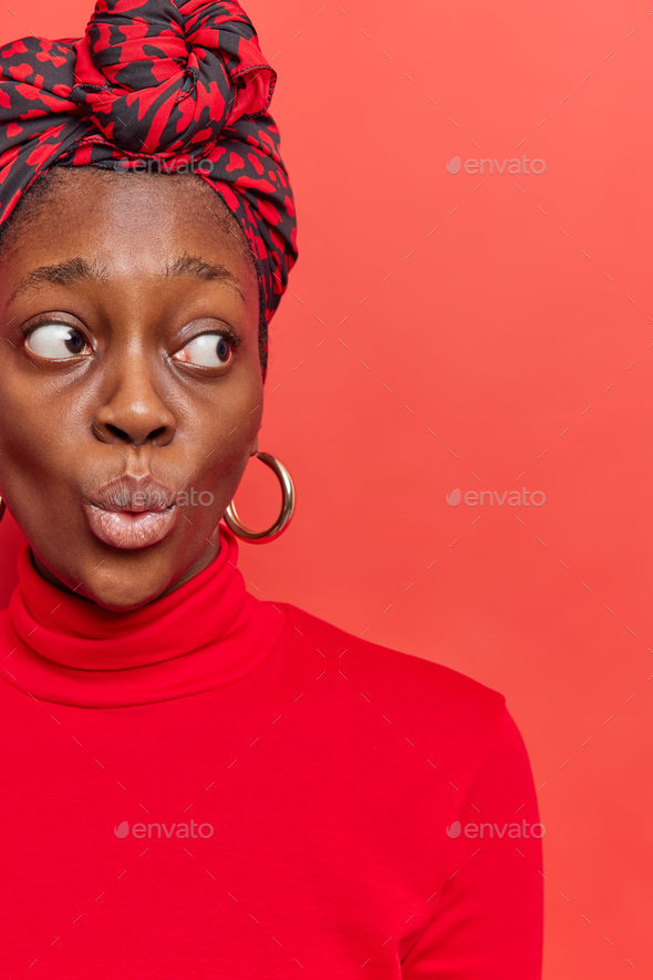 Vertical shot of scared dark skinned woman looks wondered away keeps ...