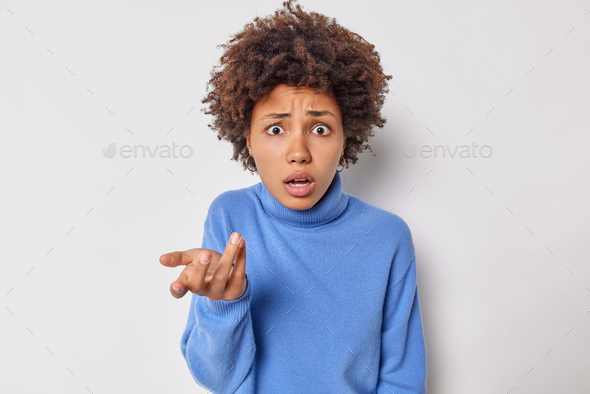 Indignant puzzled young woman shrugs shoulders has hesitant shocked ...