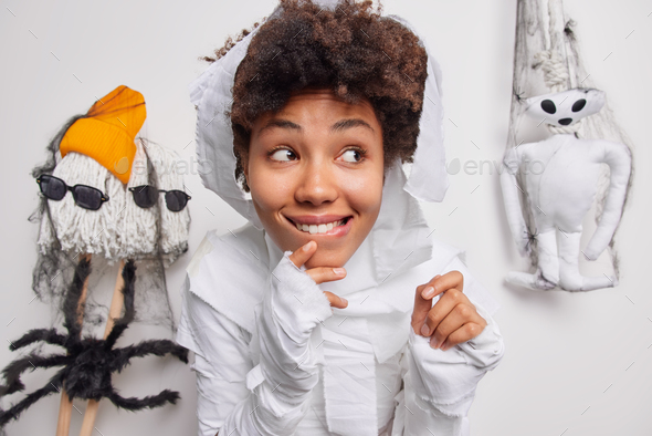 Glad ethnic woman smiles happily and looks away dressed like ghost ...