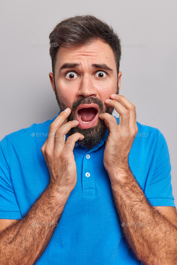 Overwhelmed bearded young man looks scared nervous grabs face keeps ...