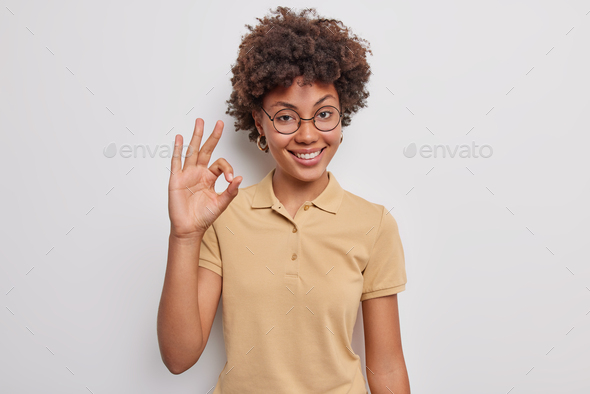 Positive young woman shows okay gesture with satisfied expression ...