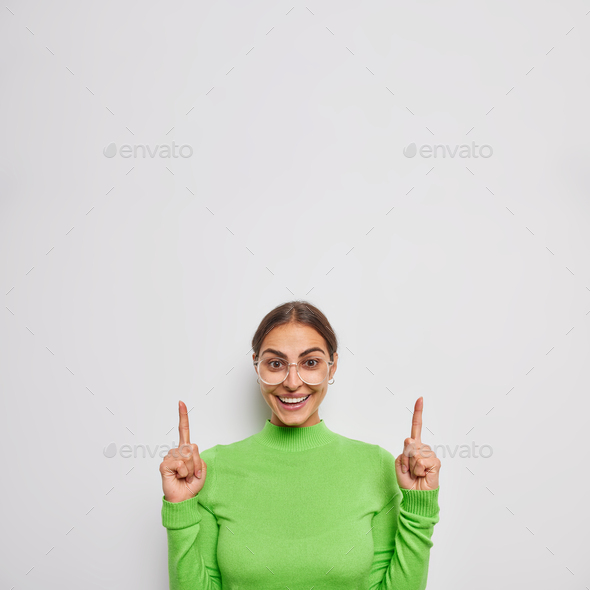 Vertical shot of positive excited young woman points fingers up points ...