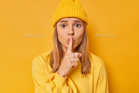 Photo of worried young female model makes shush gesture presses index ...