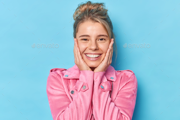 Portrait of good looking woman smiles positively keeps hands on cheeks ...
