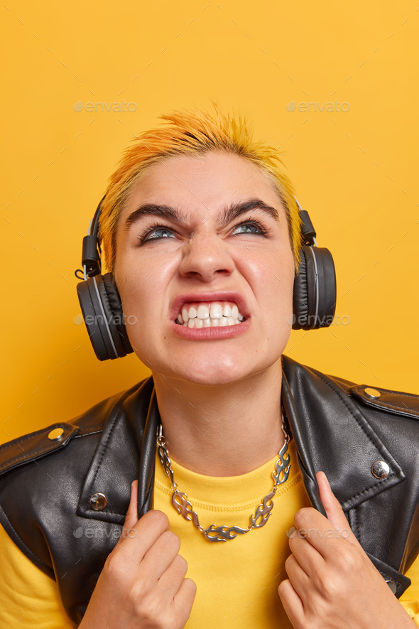 Angry female punk clenches teeth looks with irritated expression above ...