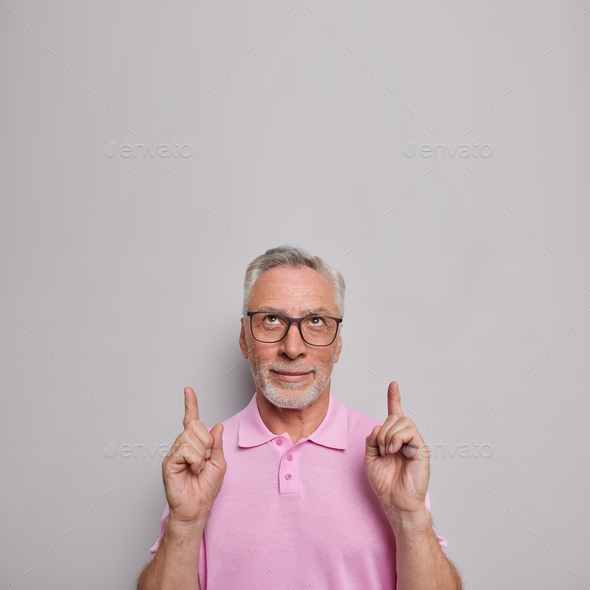Vertical shot of serious elderly man points index fingers overhead ...